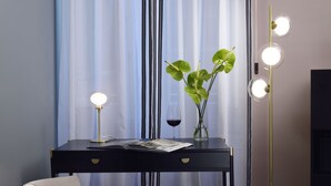 Quarto moderno com escrivaninha, cadeira, vaso com planta, taça de vinho e abajur com luzes.