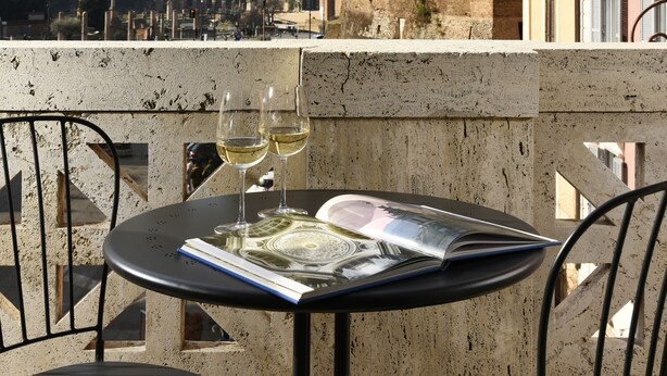 Mesa com uma revista e dois copos de vinho numa varanda com vista para um edifício histórico com uma torre.
