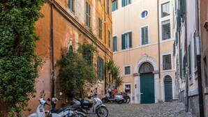 Uma rua de paralelepípedos estreita, com scooters estacionadas e edifícios antigos com portas arqueadas e persianas.