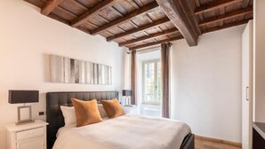 Um quarto com uma cama grande, uma mesa de cabeceira, uma obra de arte na parede e uma janela com cortinas.