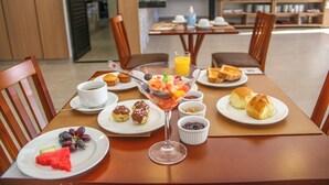Uma mesa posta para o pequeno-almoço, com diversas opções de comida, incluindo um copo de sumo de laranja, pastelaria e uma saladeira de frutas.