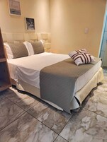 Cama bem arrumada com cabeceira, mesa de cabeceira e interruptor de luz fixado na parede.