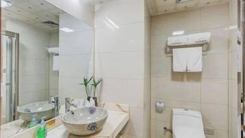 Um banheiro com toucador de mármore, pia com tigela decorativa, espelho, porta-toalhas e vaso sanitário.