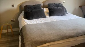 Quarto com teto inclinado, cama com cabeceira, janela com vidro jateado, unidade de ar condicionado e luminária fixada na parede.