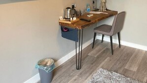Quarto pequeno e moderno com escrivaninha de madeira, uma cadeira, televisão, espelho, abajur e lixeira.