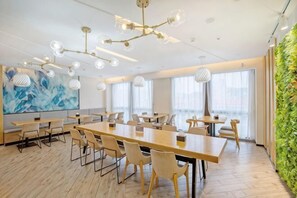 Uma sala de conferências moderna com uma mesa comprida, cadeiras, luminárias pendentes e um grande quadro abstrato na parede.