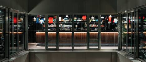 Uma área de bar moderna com divisórias de vidro, balcão e diversos elementos de iluminação.
