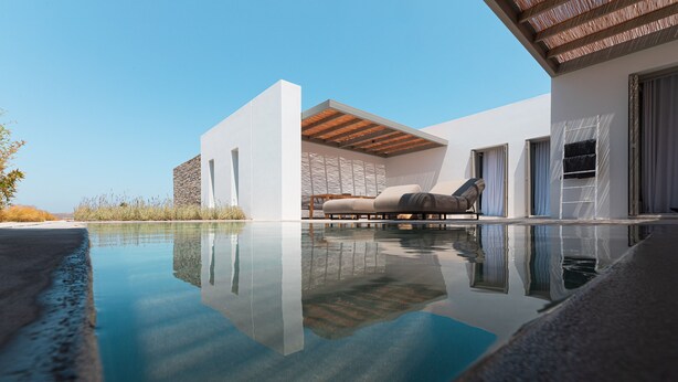 Uma área moderna à beira da piscina, com vista clara para a água, uma espreguiçadeira e um espaço de estar coberto.