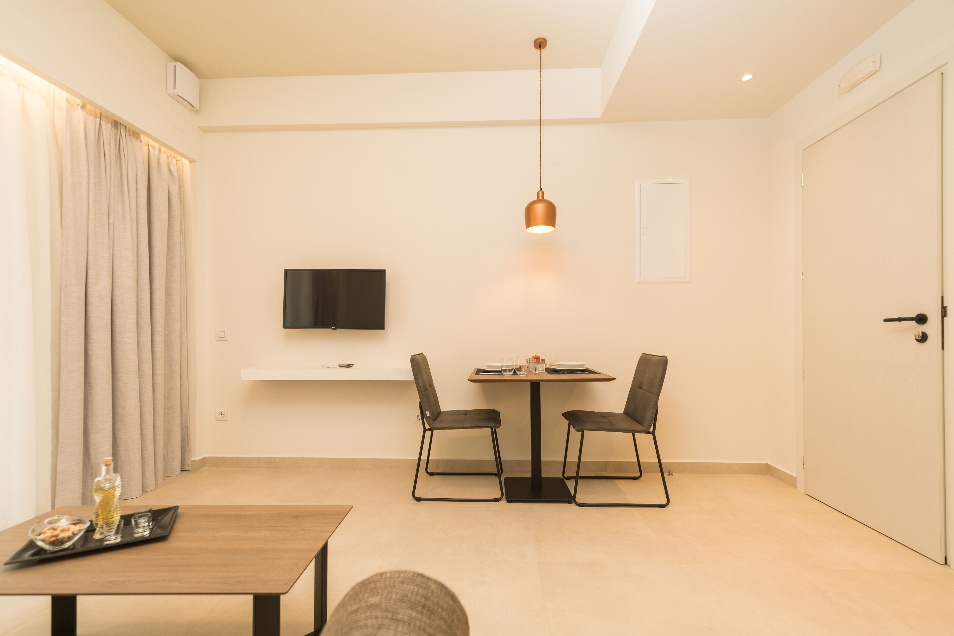 Quarto moderno com uma mesa de jantar, duas cadeiras, uma TV fixada na parede e uma porta.