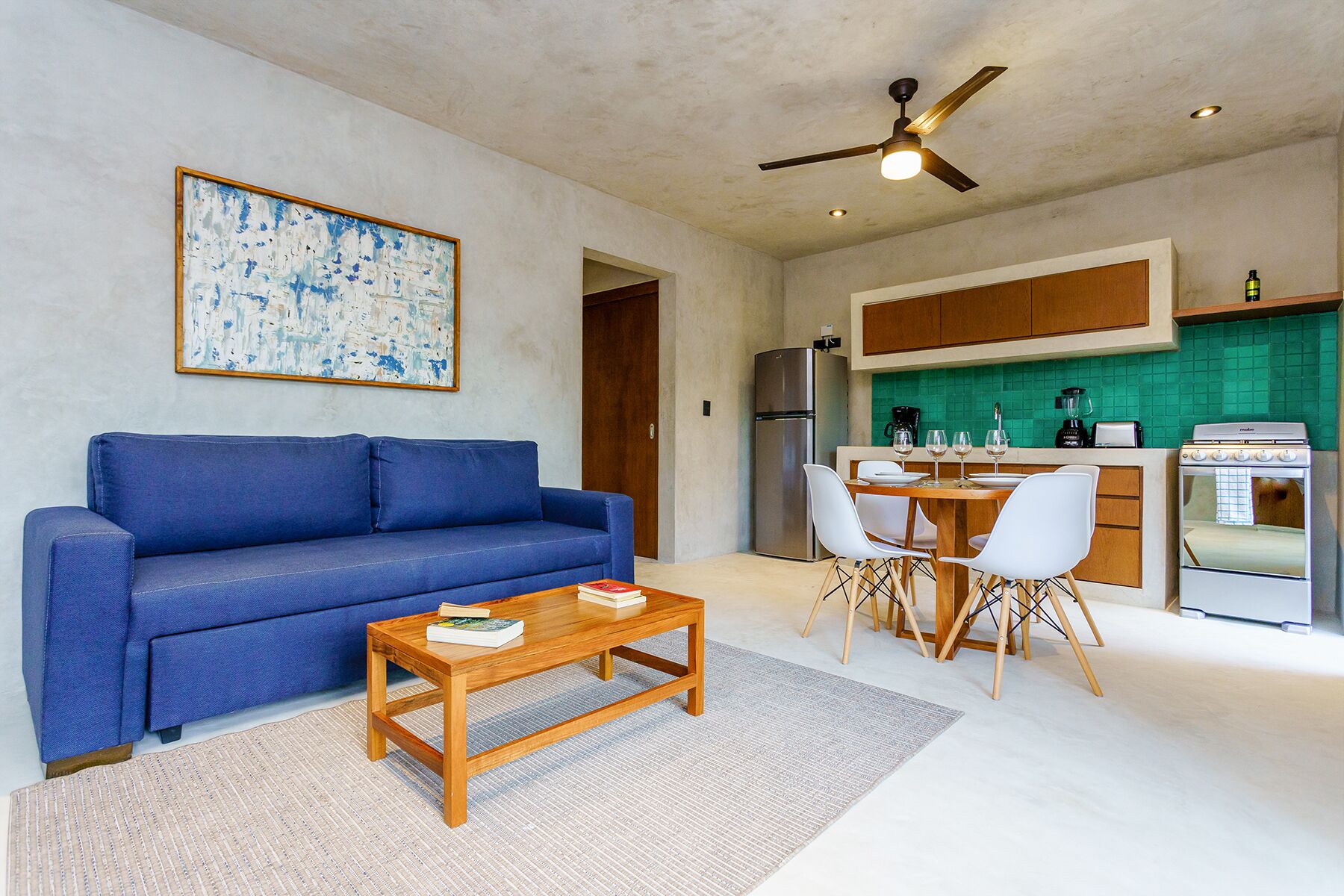 Uma sala de estar moderna com um sofá azul, uma mesa de centro de madeira e um espaço de jantar com cadeiras brancas e uma mesa de madeira.