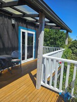 Um deck de madeira com uma porta azul, corrimão branco e um regador azul.