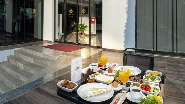 Entrada de hotel com mesa de buffet ao ar livre, servindo itens de café da manhã.