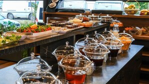 Buffet variado com diversas opções de alimentos e bebidas, incluindo frutas, legumes e refrescos.