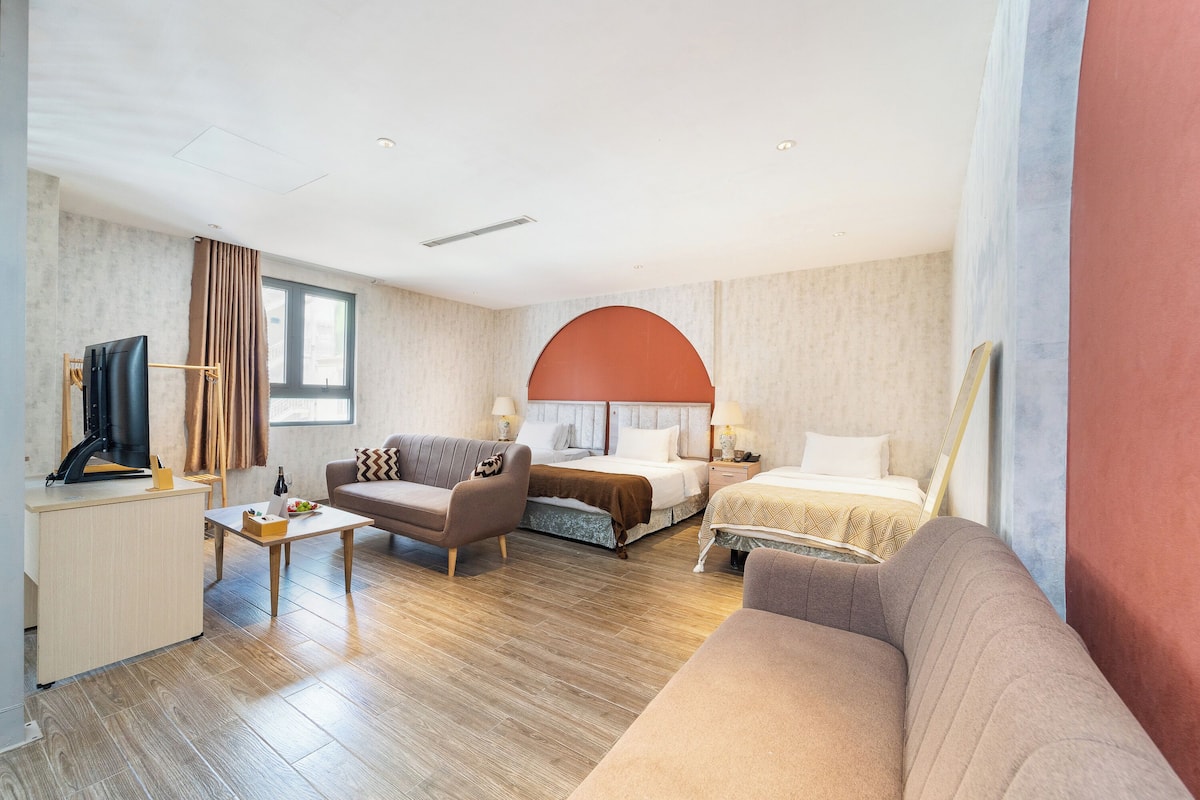 Quarto de hotel com cama, dois sofás, escrivaninha e televisão.