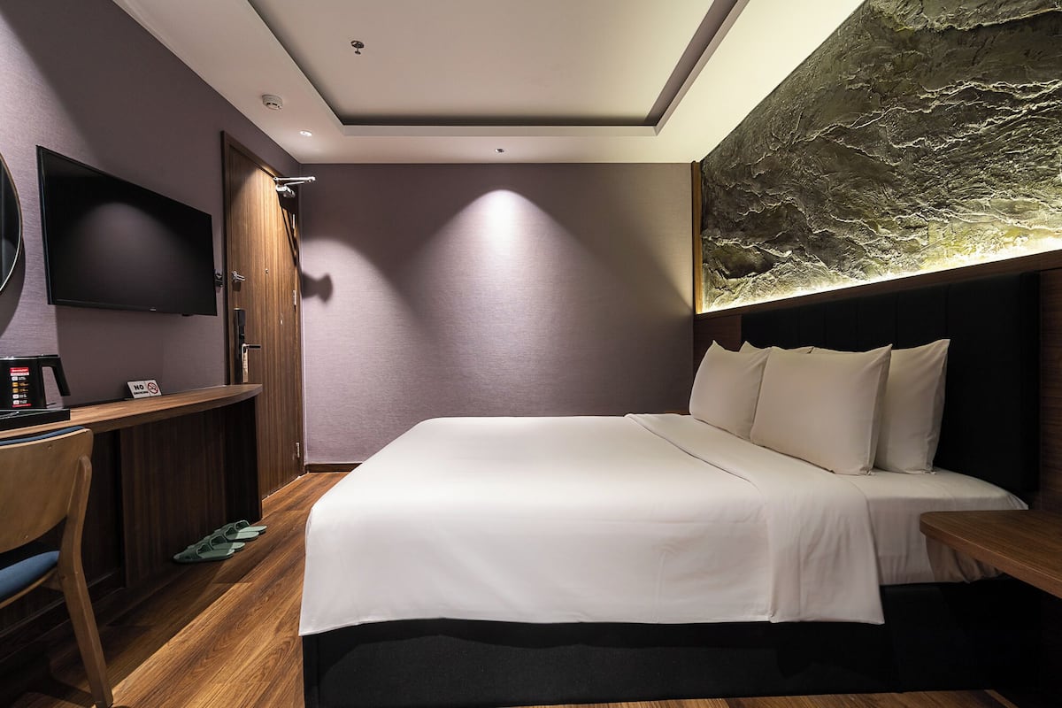 Quarto de hotel com uma cama grande, televisão de tela plana na parede, secretária de madeira com cafeteira e uma obra de arte pendurada na parede.