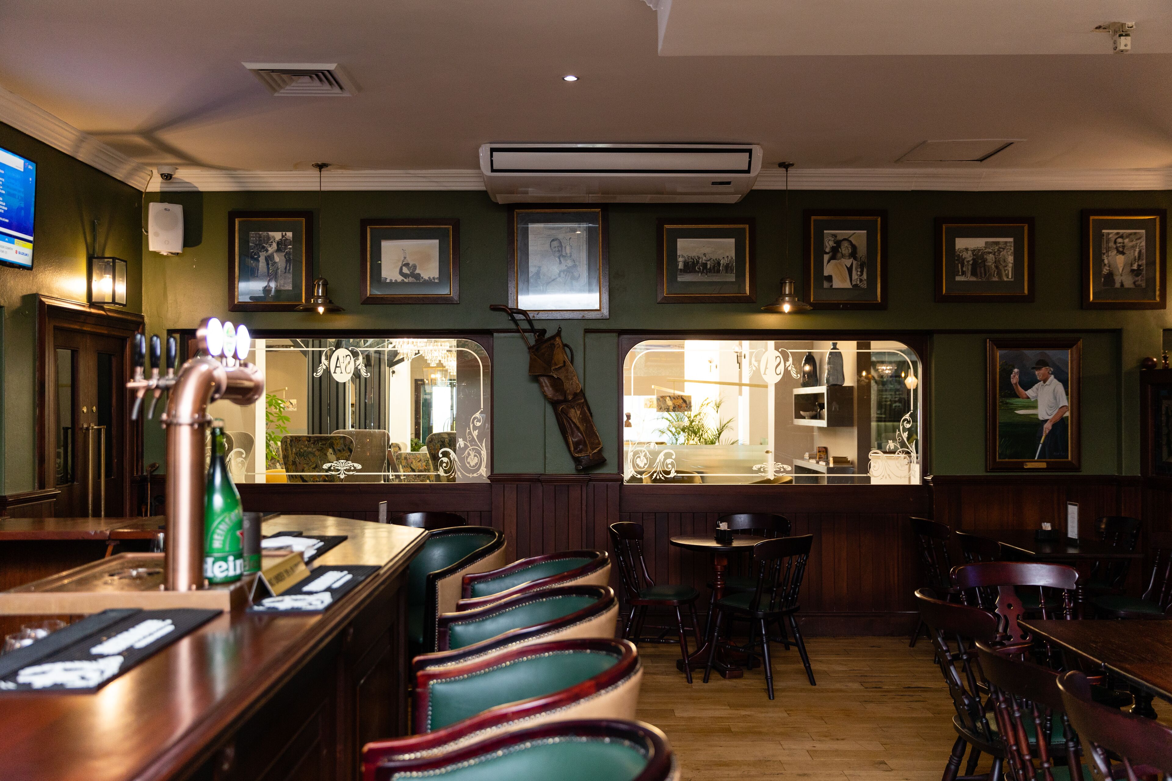 Interior de restaurante com mesas e cadeiras de madeira, área de bar com torneiras e quadros nas paredes.
