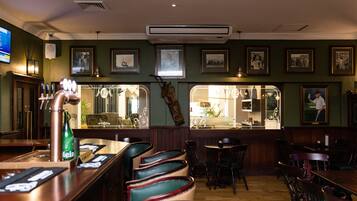 Interior de restaurante com mesas e cadeiras de madeira, área de bar com torneiras e quadros nas paredes.