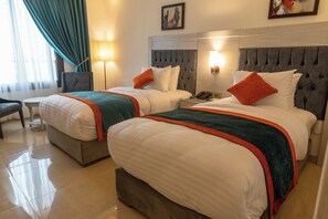 Quarto de hotel com duas camas, uma mesinha de cabeceira, uma cadeira e um abajur.