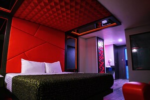 Quarto de hotel moderno com uma parede de destaque vermelha, uma cama grande com roupa de cama branca e uma poltrona vermelha.