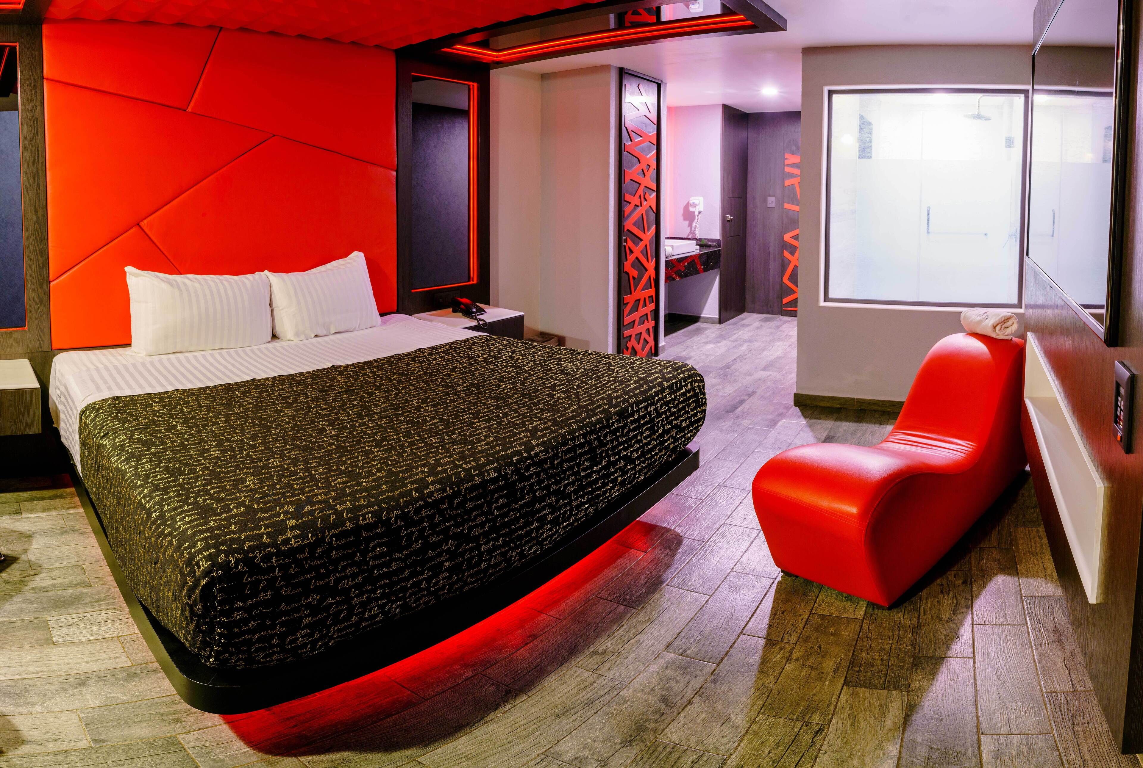 Quarto de hotel moderno com uma cama grande, uma cadeira vermelha e uma janela ampla.