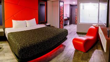 Quarto de hotel moderno com uma cama grande, uma cadeira vermelha e uma janela ampla.