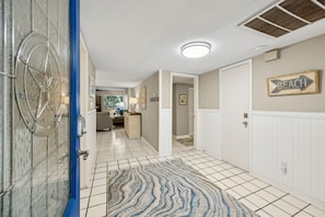 Um corredor com piso de azulejos, porta azul, tapete estampado e uma placa na parede com a inscrição 'BEACH'.