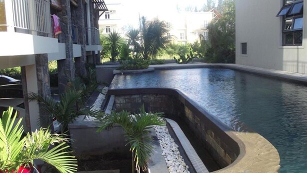 Piscina com borda curva, rodeada por vegetação e edifícios.