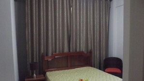 Quarto de hotel com uma cama, mesa de cabeceira, uma cadeira e uma janela com cortinas.