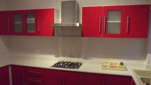 Uma cozinha com armários vermelhos, fogão a gás e exaustor de aço inoxidável.