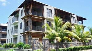 Hotel de vários andares com varandas, parede de pedra e plantas tropicais.
