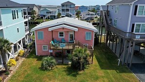 Uma casa rosa com varanda, rodeada por outras casas e um deck de madeira.
