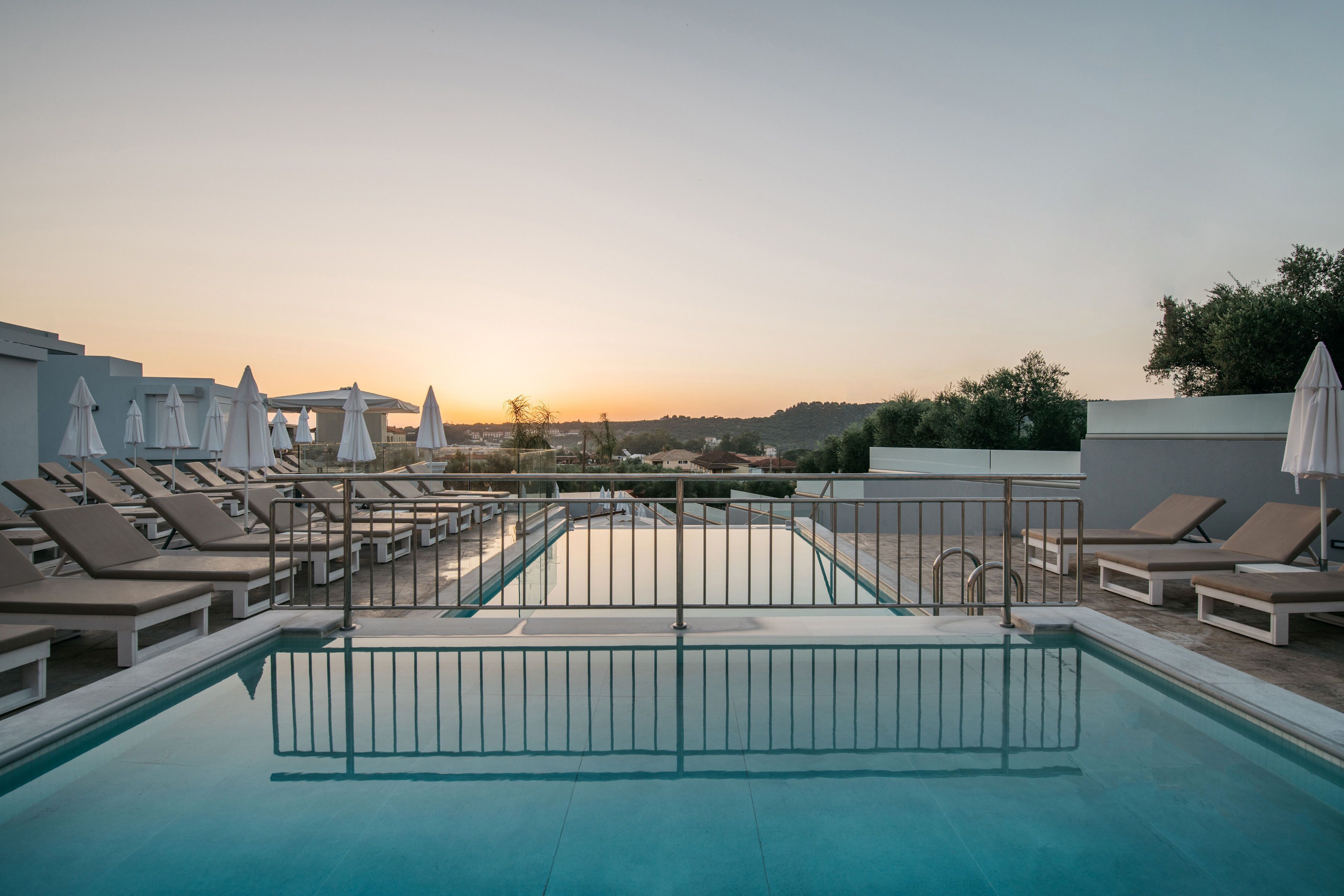 Piscina no terraço com espreguiçadeiras e guarda-sóis, cercada por uma grade de metal.