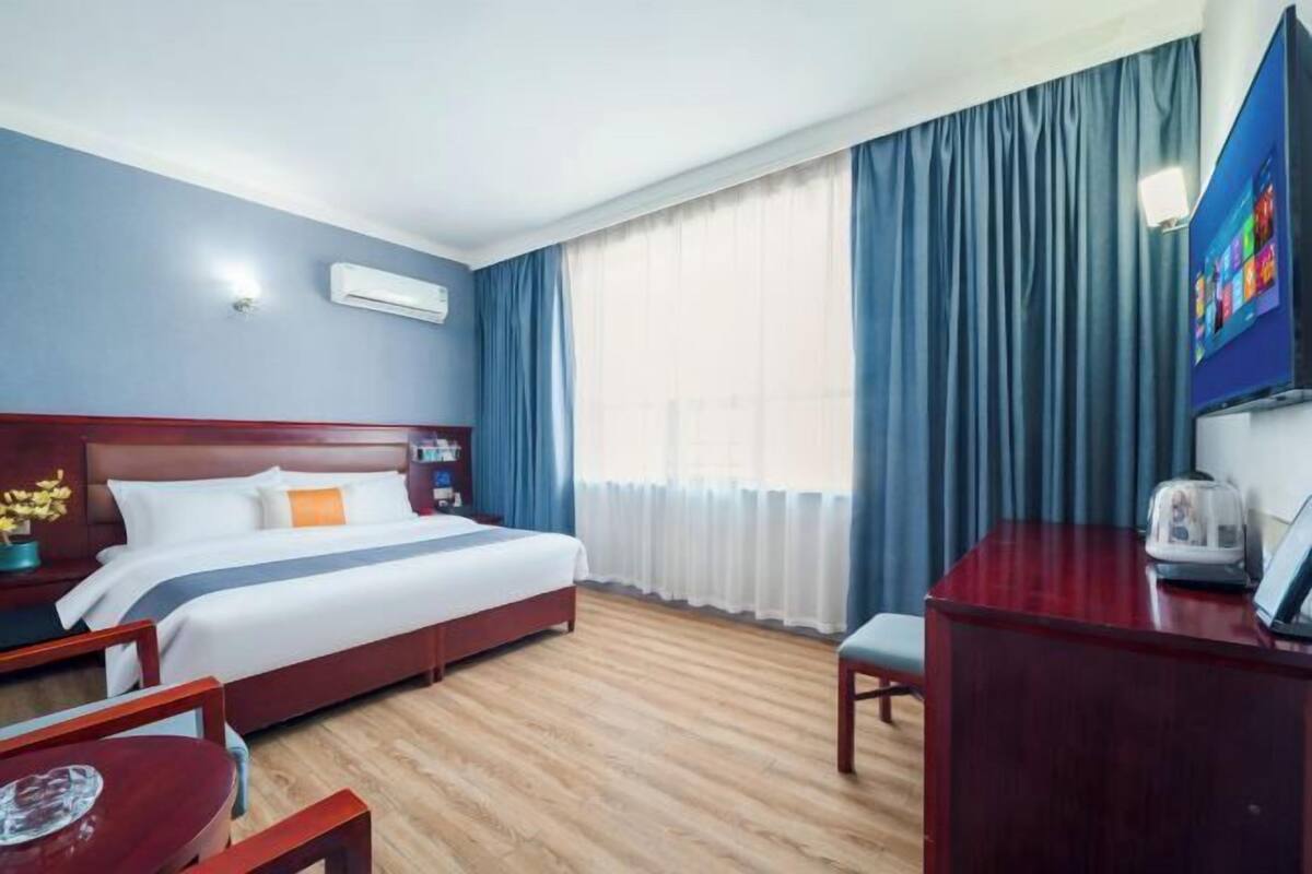 Quarto de hotel com cama, escrivaninha, cadeira, mesinha e televisão.