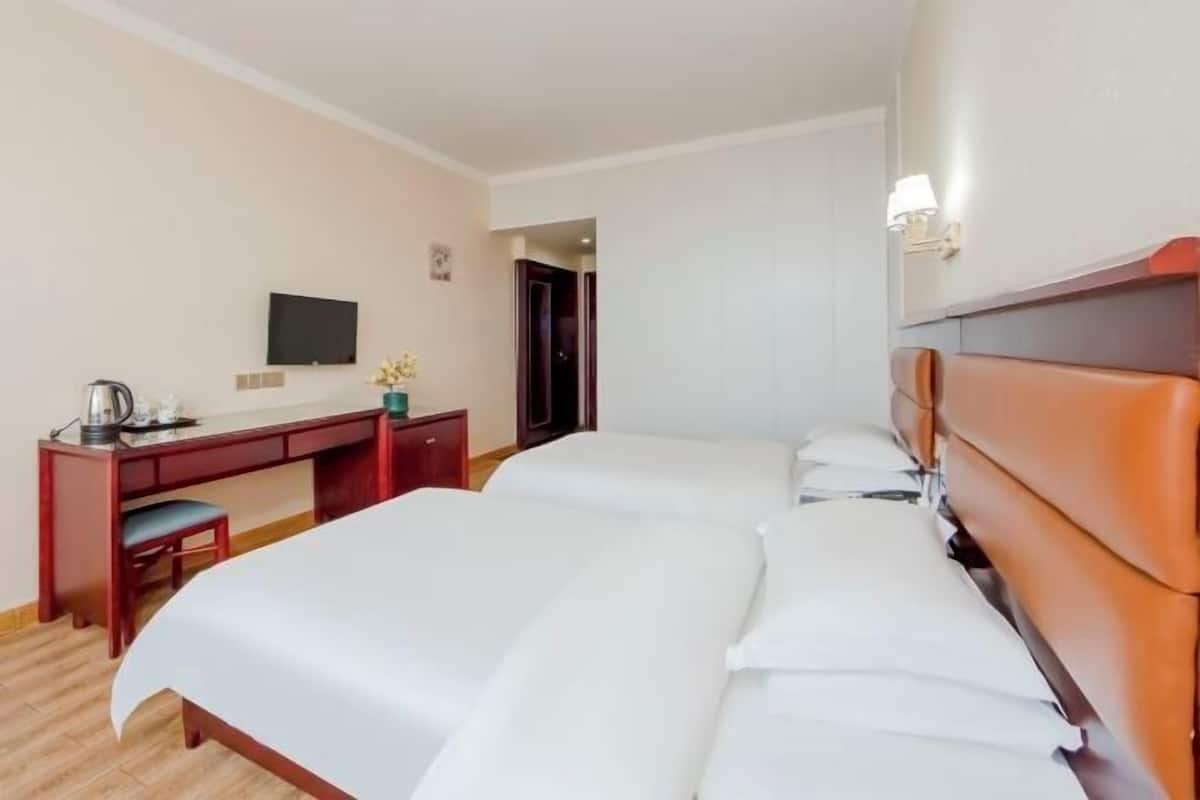 Quarto de hotel com uma cama grande, uma escrivaninha com cadeira, uma televisão e um abajur.