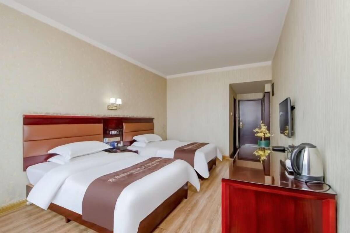 Quarto de hotel com duas camas, cabeceira de madeira, escrivaninha com espelho e cafeteira.