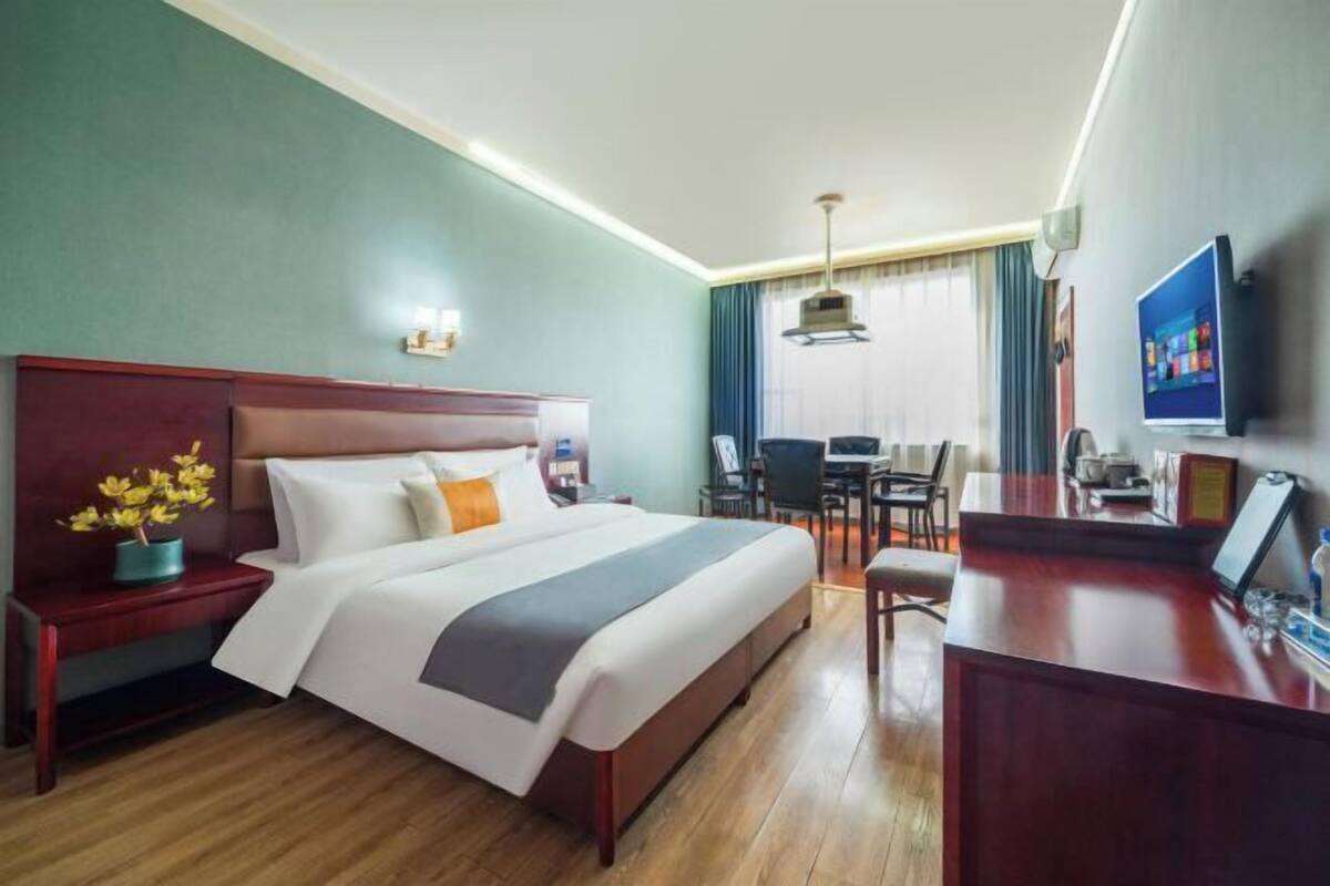 Quarto de hotel com uma cama grande, uma escrivaninha e uma televisão.