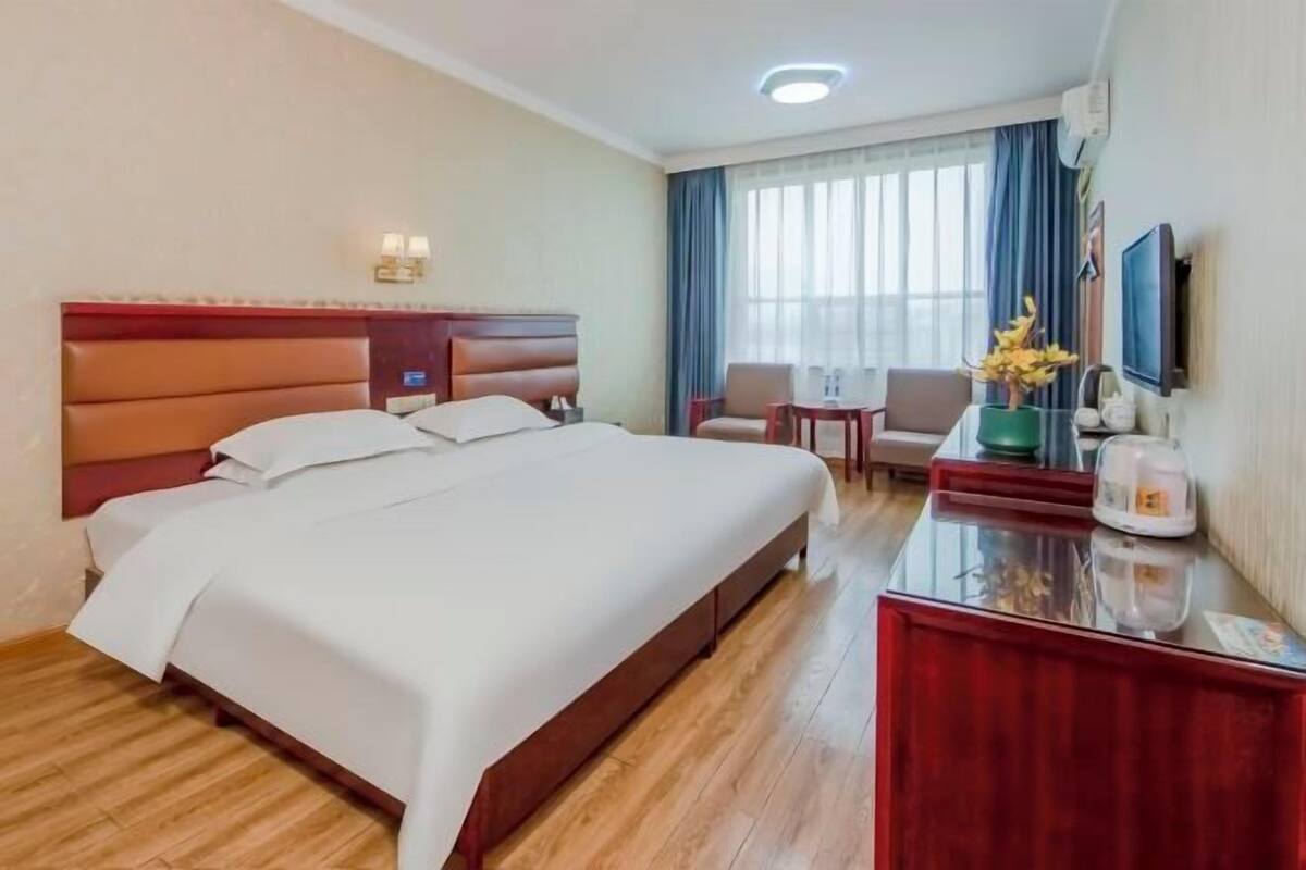 Quarto de hotel com uma cama grande, uma escrivaninha com cadeira, televisão e uma janela com cortinas.