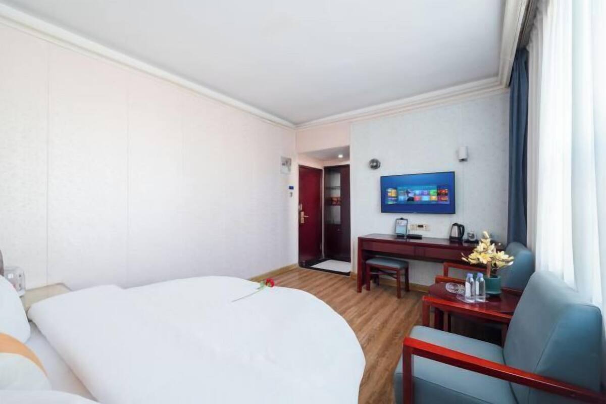 Quarto de hotel com cama, escrivaninha, cadeira, televisão e janela.