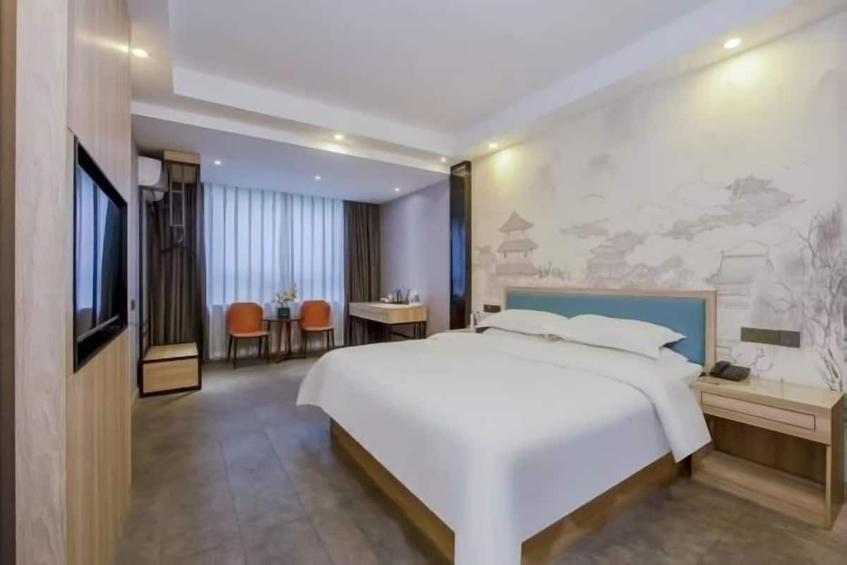 Quarto de hotel com uma cama grande, mesas de cabeceira, uma escrivaninha com cadeiras e vista para um edifício tradicional pela janela.