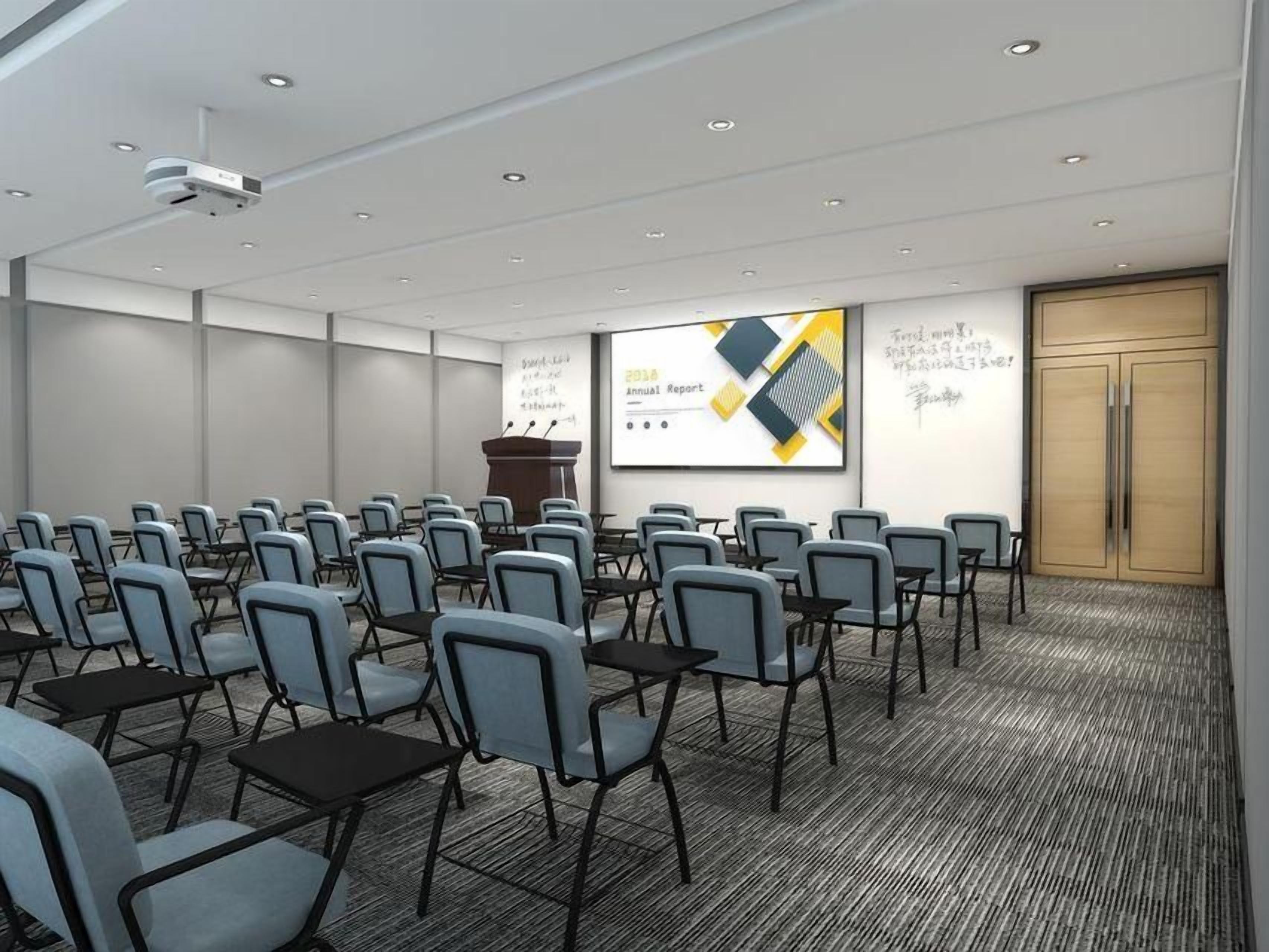 Uma sala de conferências com fileiras de cadeiras e mesas, uma tela de projeção exibindo uma apresentação e um púlpito.