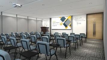 Uma sala de conferências com fileiras de cadeiras e mesas, uma tela de projeção exibindo uma apresentação e um púlpito.