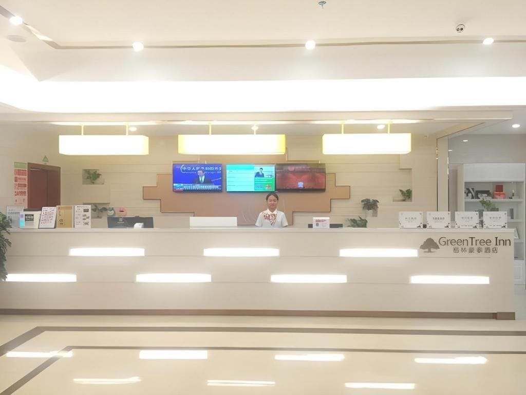Uma mesa de recepção com um visor digital, a placa da GreenTree Inn e uma planta no balcão.