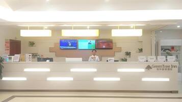 Uma mesa de recepção com um visor digital, a placa da GreenTree Inn e uma planta no balcão.