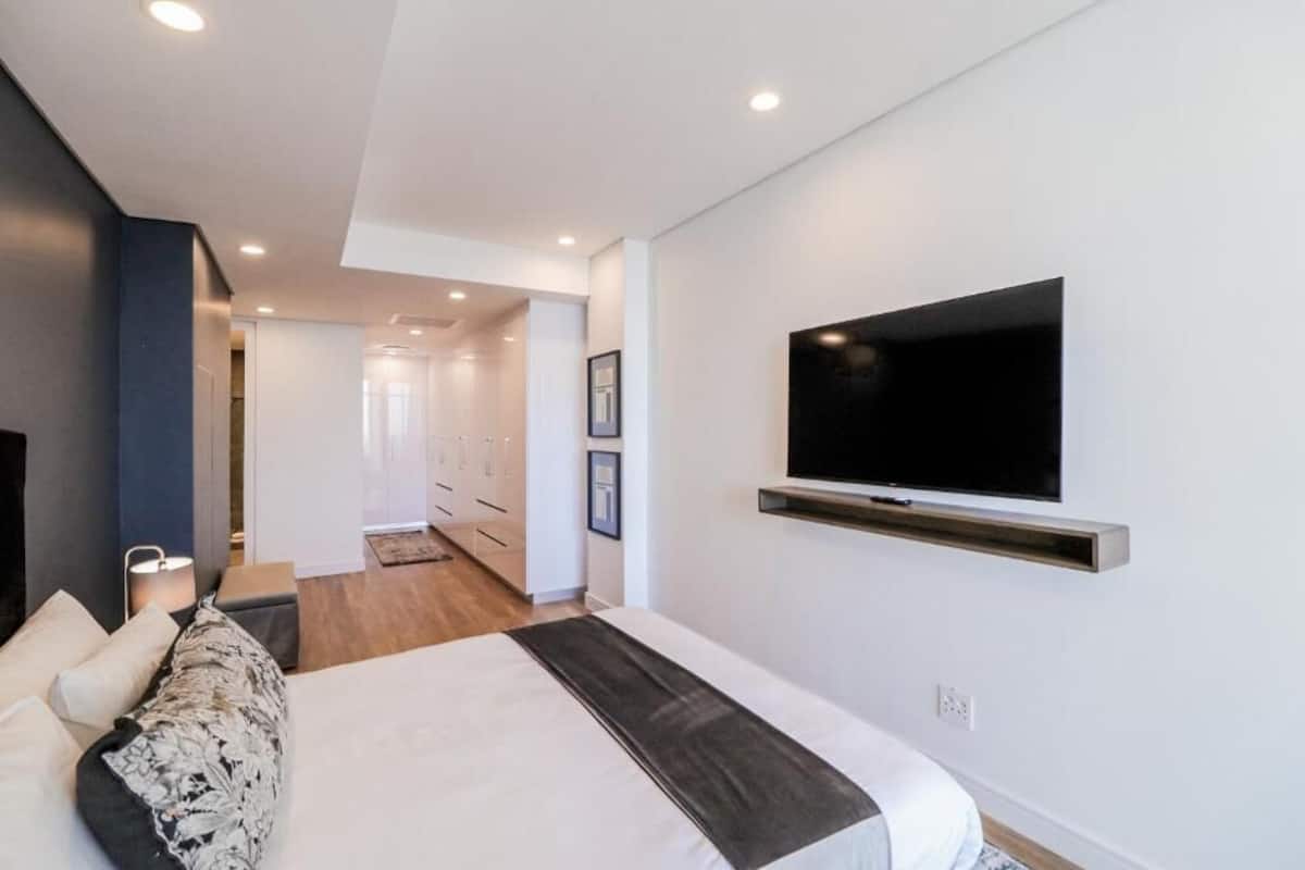 Quarto de hotel moderno com uma cama grande, televisão montada na parede e um closet espaçoso.