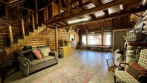 Um amplo loft com pé direito alto, vigas de madeira aparentes, escada, sofá, poltrona e tapete.