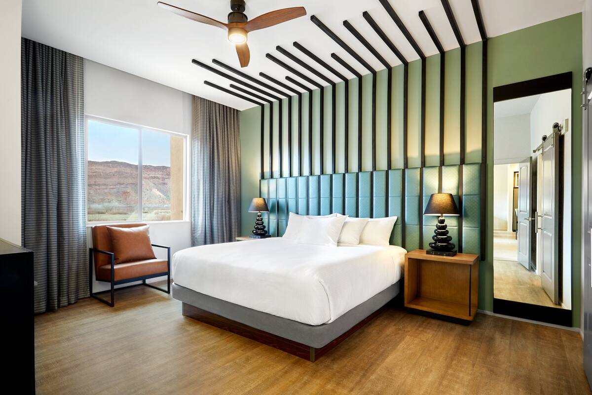 Quarto de hotel moderno com uma cama grande, uma cadeira, uma mesa de cabeceira e um espelho.