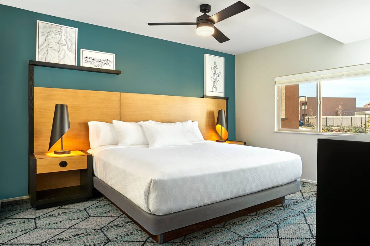 Quarto moderno com cama grande, cabeceira de madeira, duas luminárias de cabeceira e ventilador de teto.