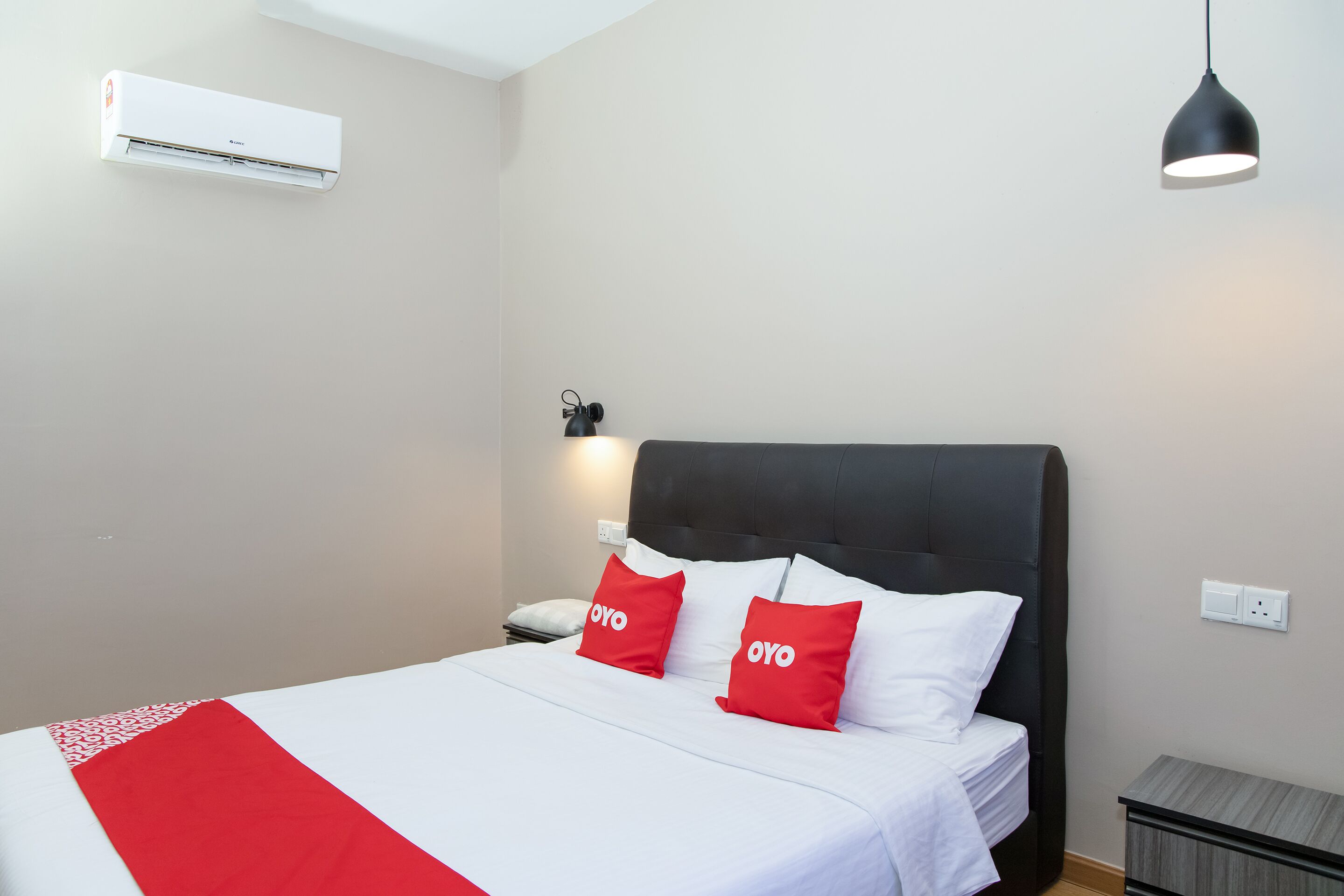 Quarto de hotel com cama, mesa de cabeceira, luminária e ar condicionado.