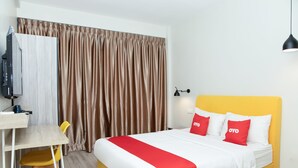 Quarto de hotel com cama, escrivaninha, cadeira, televisão e cortinas.
