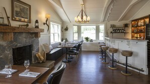 Um quarto amplo com uma mesa de jantar comprida, área de bar e assentos junto às janelas.